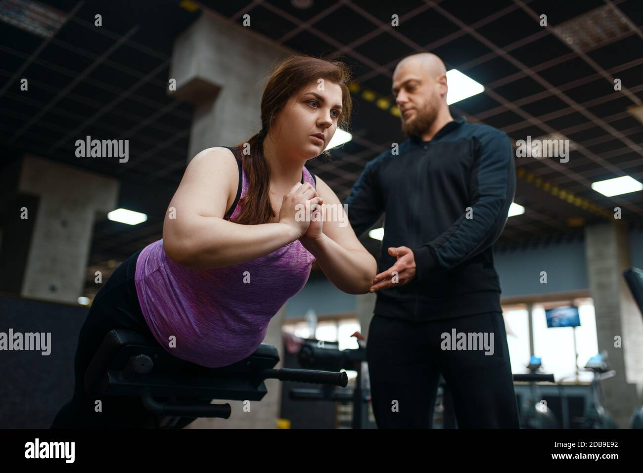 Trainer helps to overweight woman on exercise machine, gym. Female ...