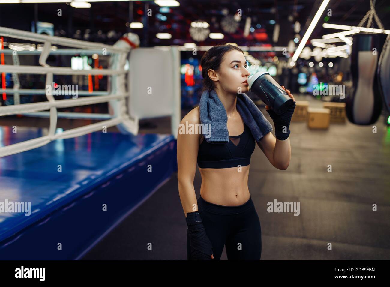 Woman in black boxing bandages drinks water at the ring, box training ...