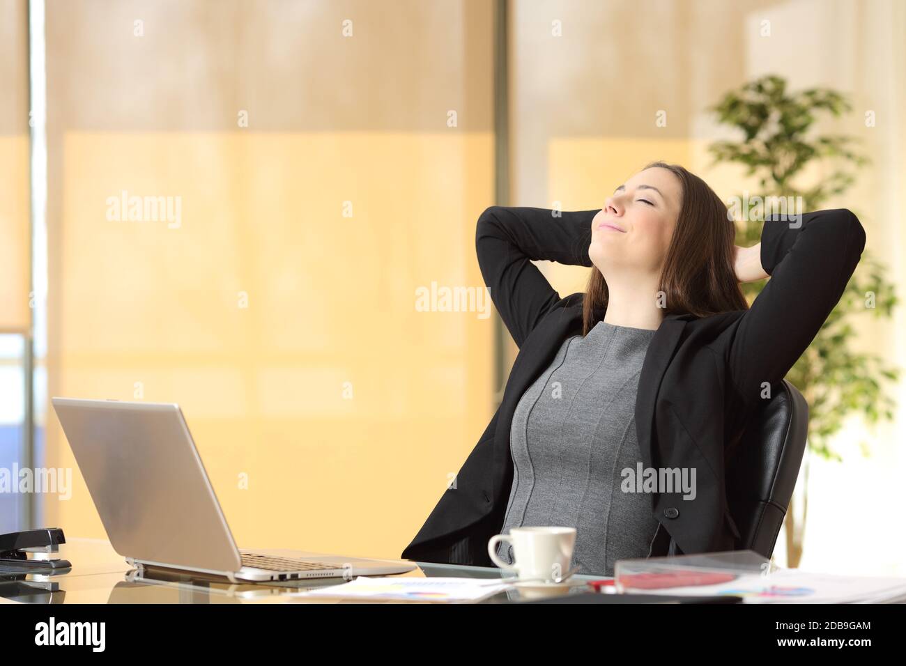 Relaxed executive woman breathing fresh air with arms on head on a desk ...