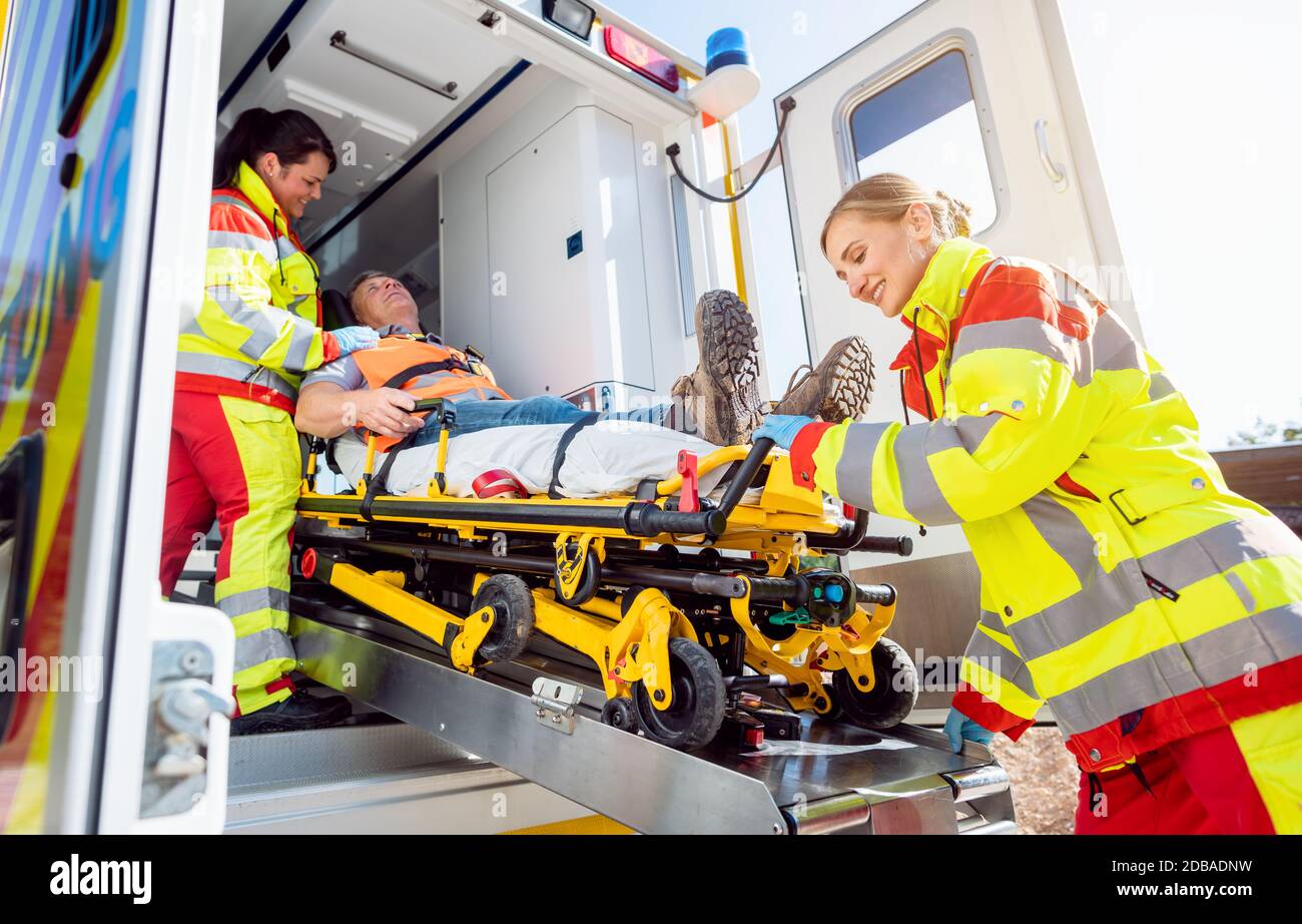 Paramedics in uniform putting injured man on stretcher in ambulance car ...
