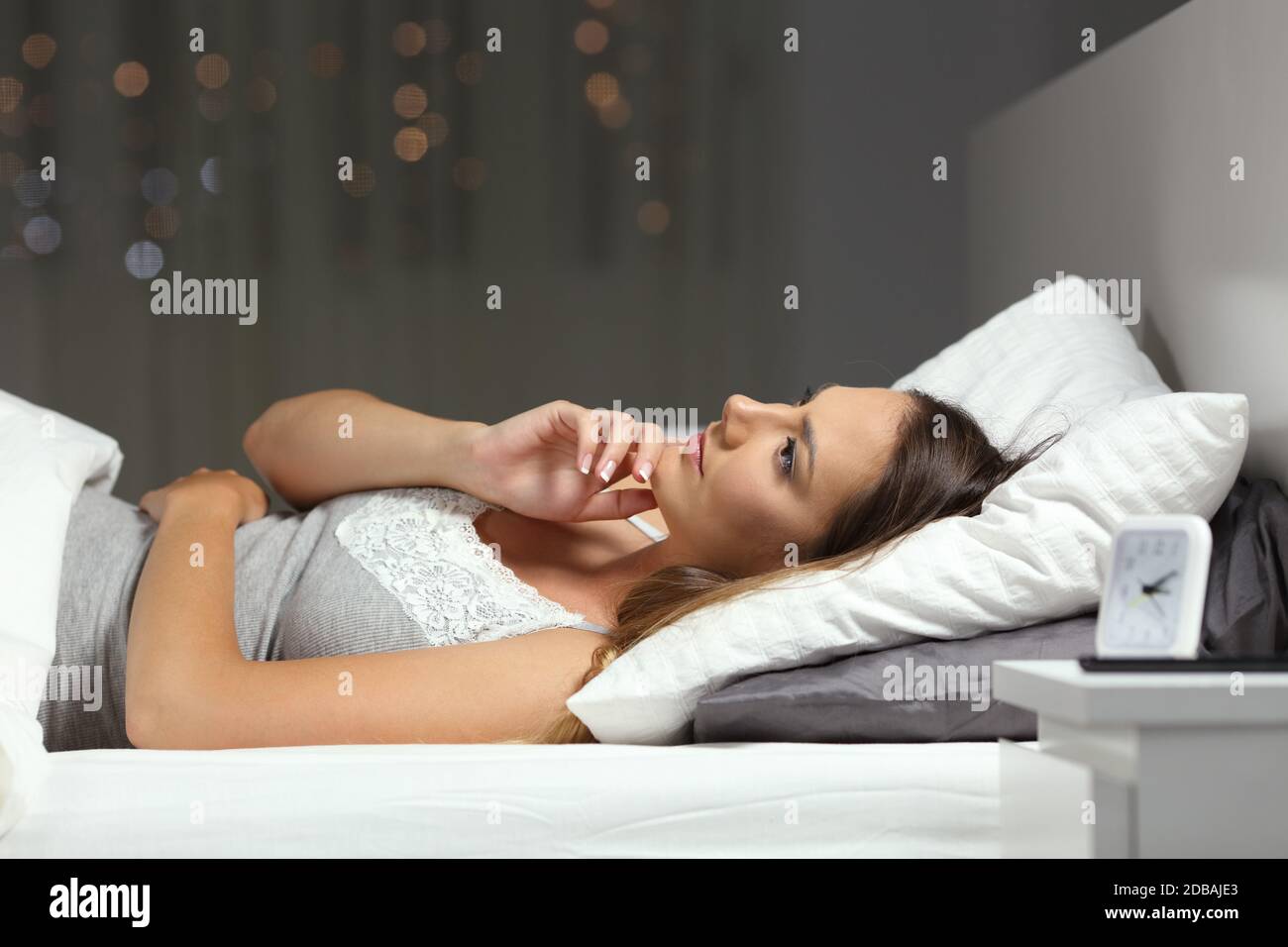 Pensive serious woman thinking lying on the bed in the night at home ...