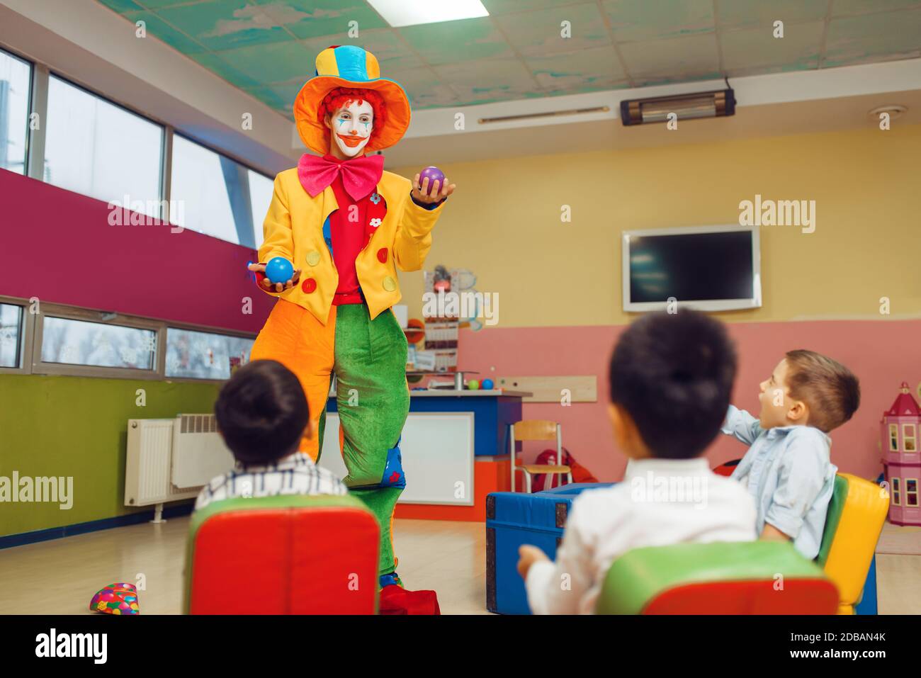 Funny clown juggles in front of surprised children. Birthday party ...