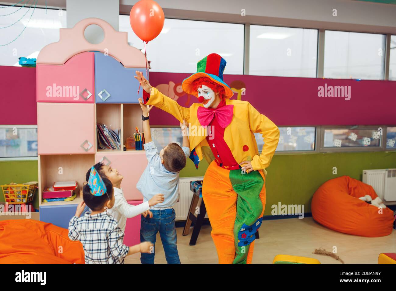 Funny clown shows tricks with balloon to surprised children. Birthday ...
