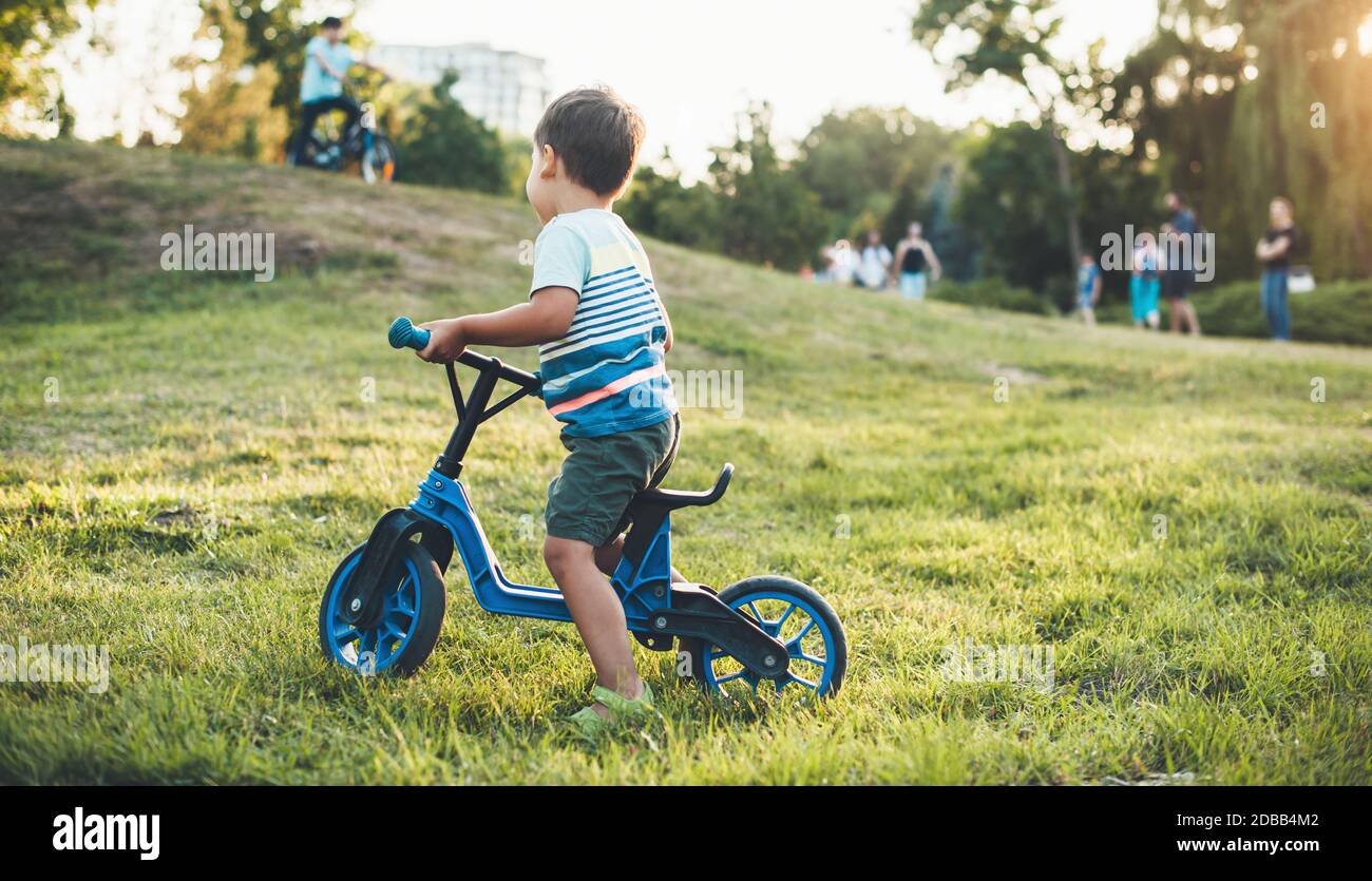Small boy riding a bike in the park looking at other children walking ...