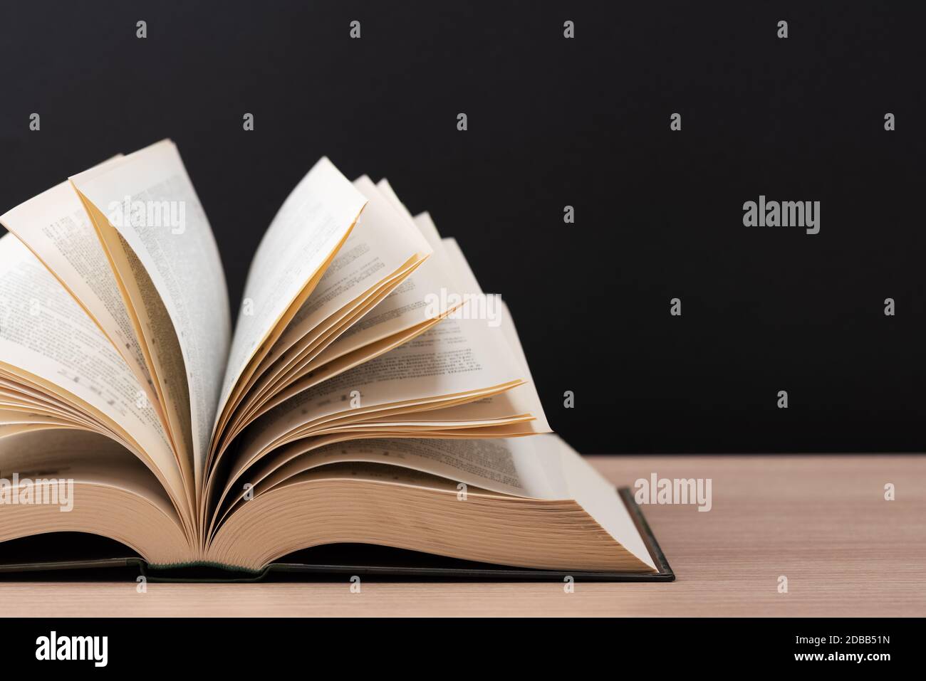 A large, thick hardcover book lies on a light-wood table. The book is ...