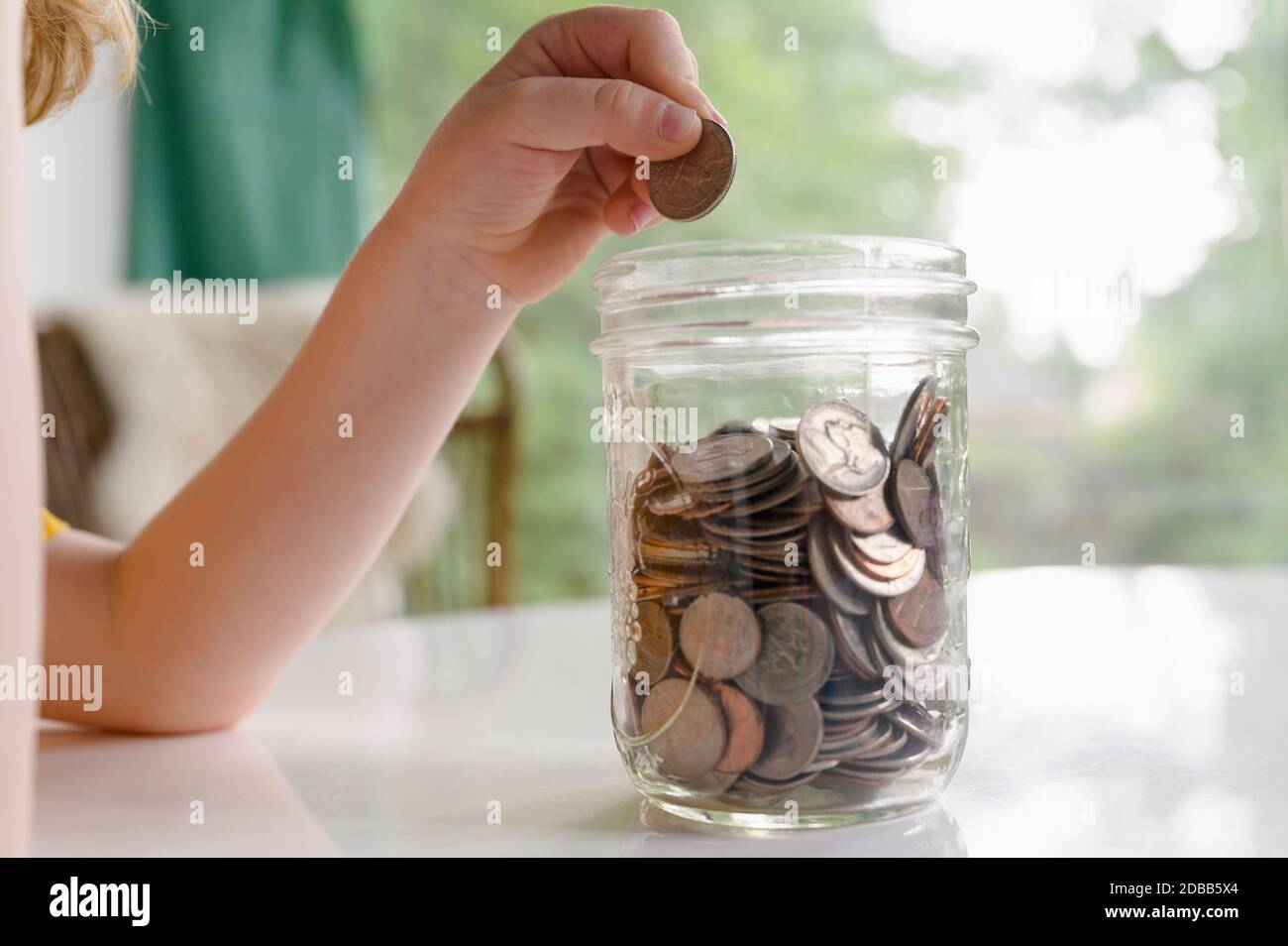 Boys (4-5) hand putting coins into jar Stock Photo - Alamy