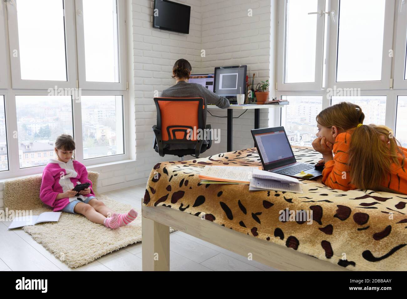 two children and an adult work in different electronic devices at home ...