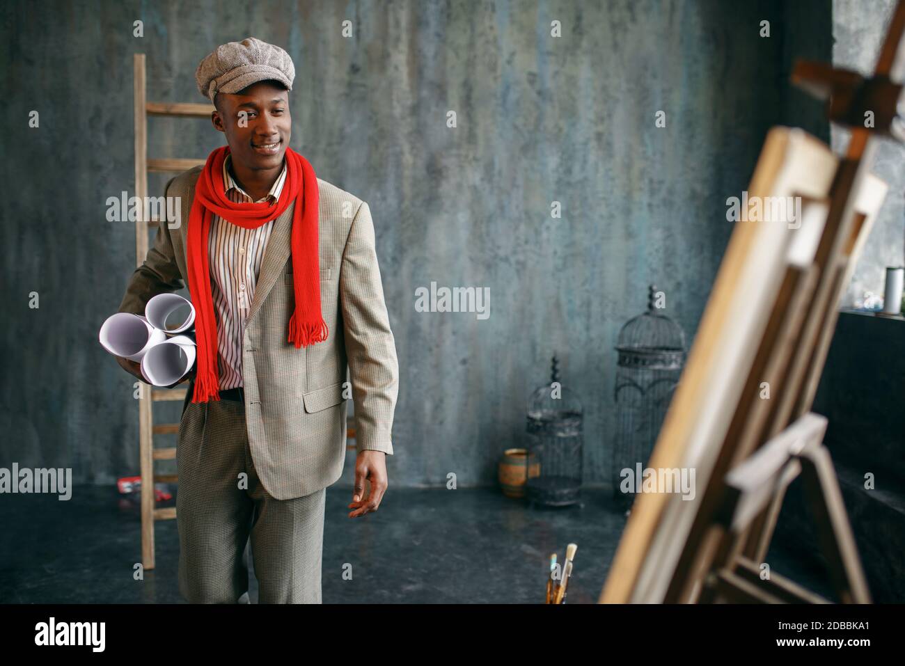 Happy male painter with rolls of canvases poses at the easel in art ...