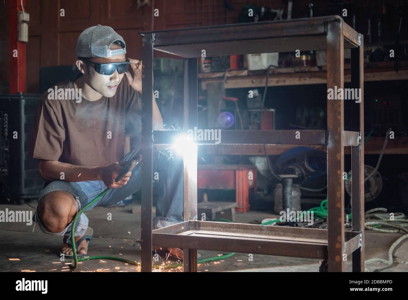 Squat welder wearing black welding glasses to make iron racks in welding workshops Stock Photo ...
