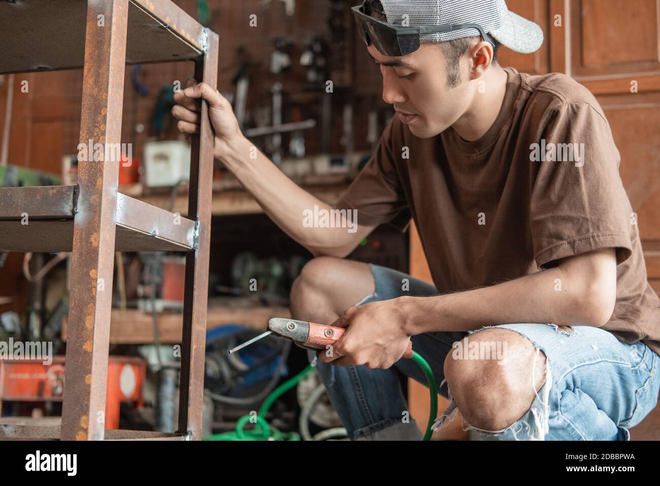 Asian welder holds an iron rack when welding using an electric welder ...