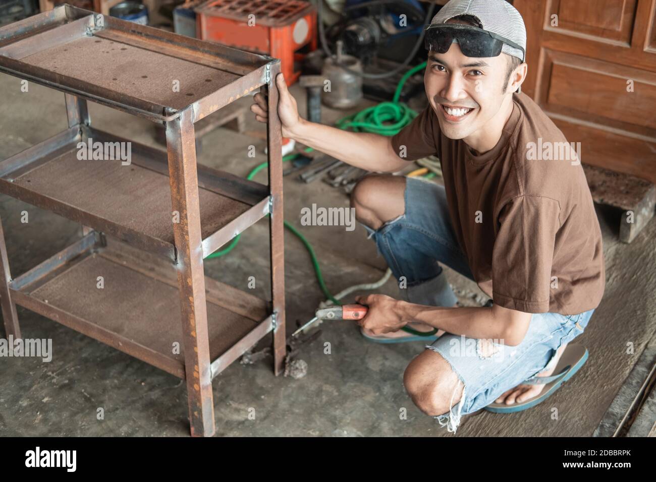 Asian welder smiles at the camera holding an iron rack while welding ...