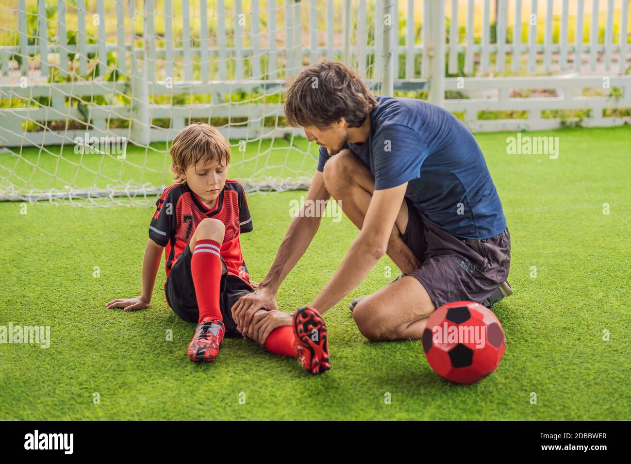 Little cute kid boy in red football uniform and his trainer or father ...