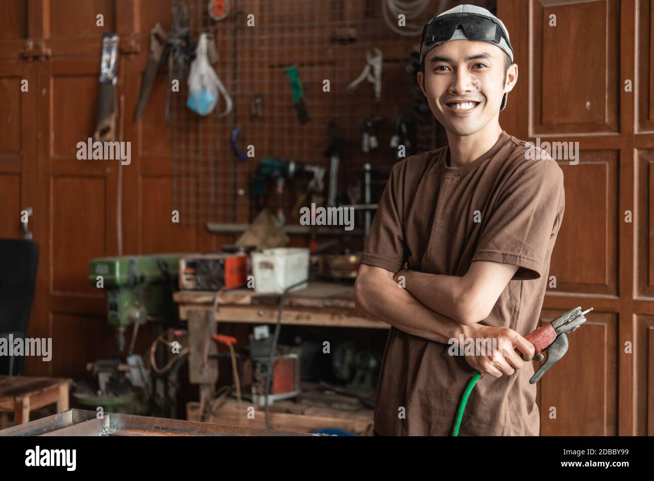 Male welder smiles with crossed hands while holding electric welder in ...