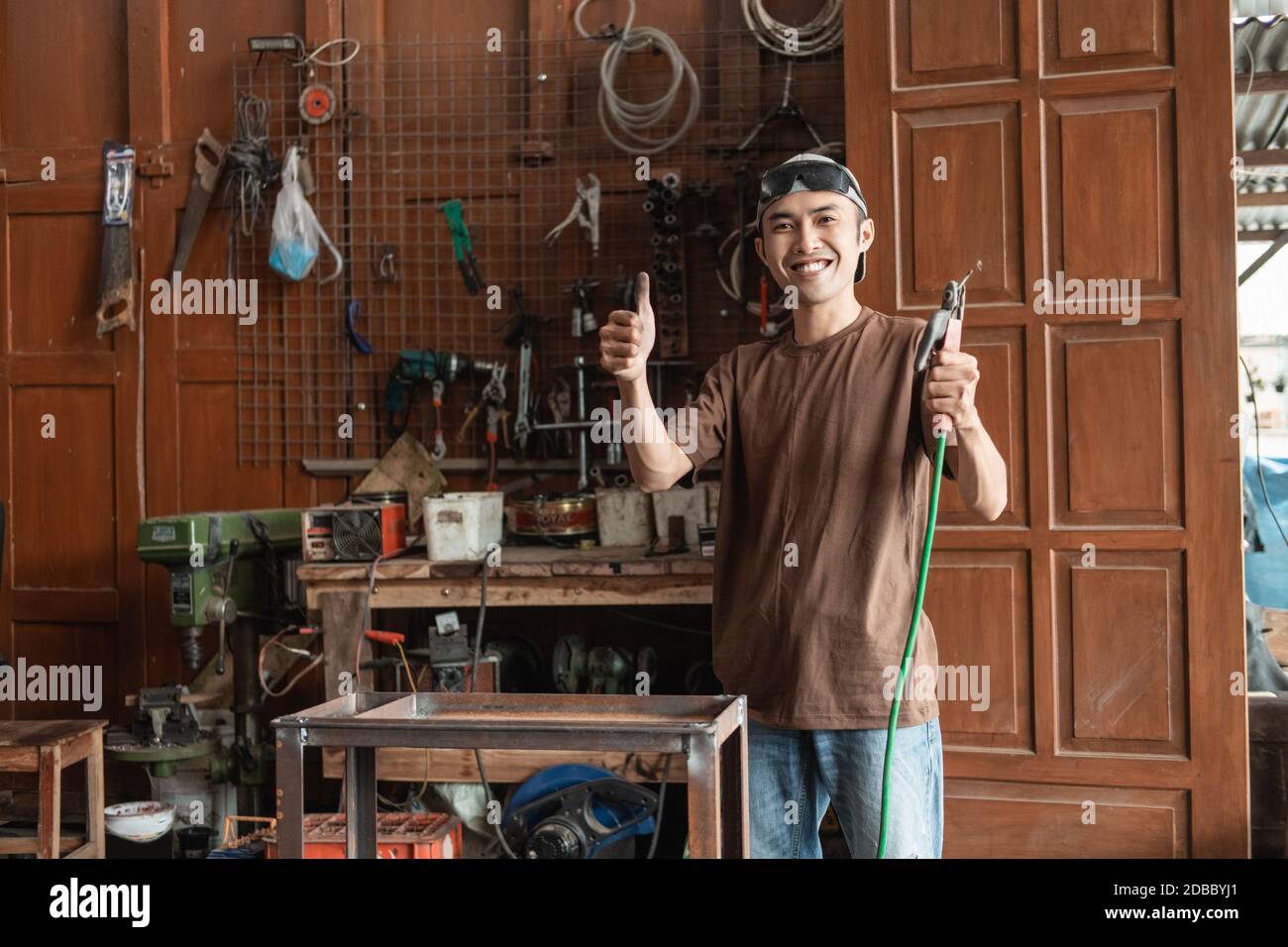 Asian male welder smiles with a thumbs up while holding an electric ...