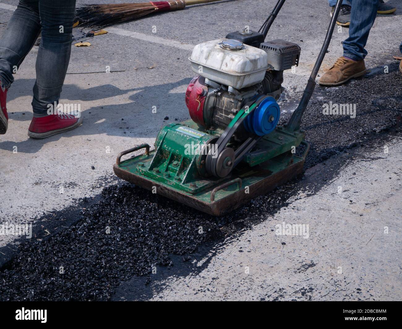 Worker use vibratory plate compactor compacting asphalt at road repair ...