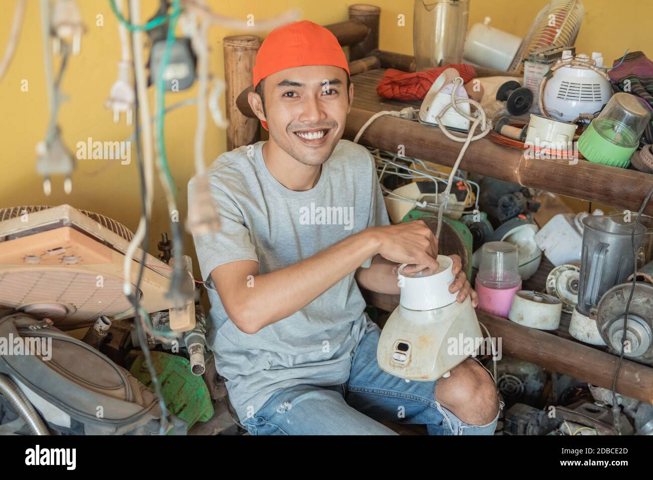 electronics repairman smiles at the camera while holding a broken ...
