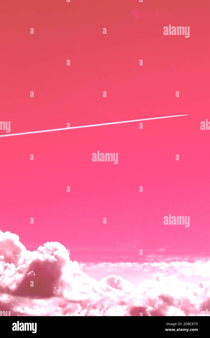 The trail of a flying airplane in a clear pink sky over large clouds ...