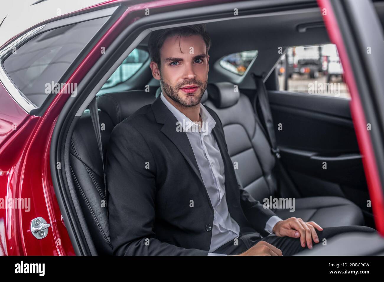 Brown-haired male sitting at backseat of red car Stock Photo - Alamy