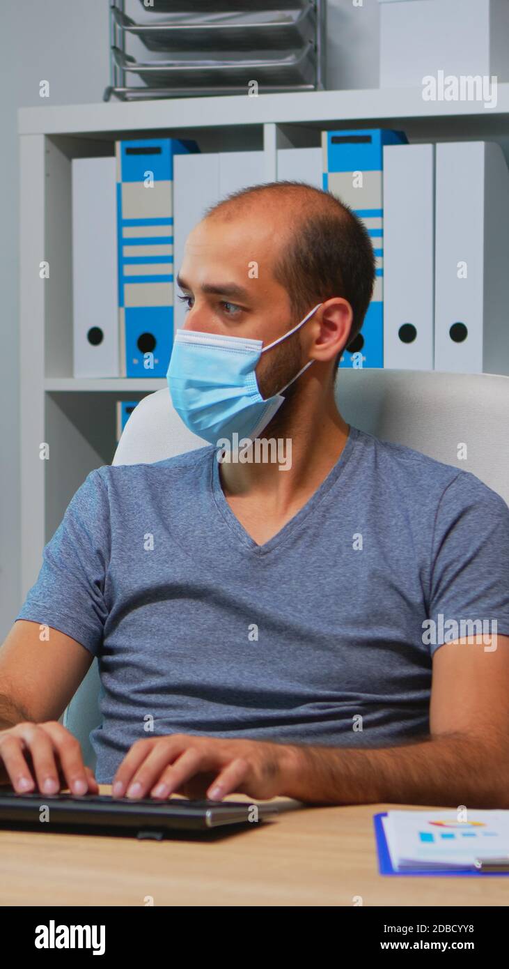Businessman with medical protection face mask typing on computer in ...