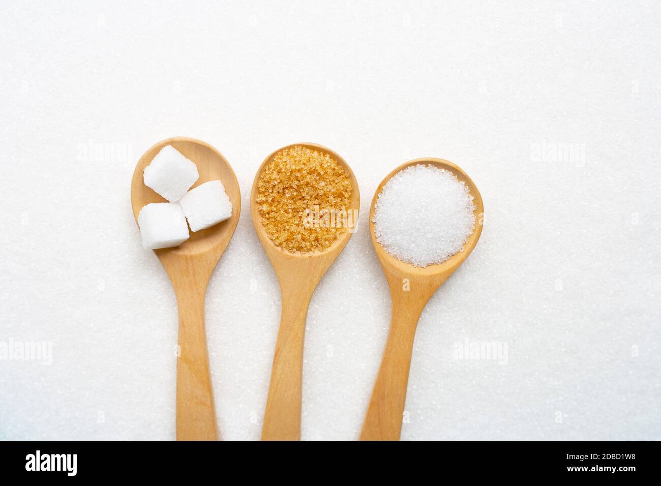 Wooden spoon with various types of sugar on white granulated sugar ...