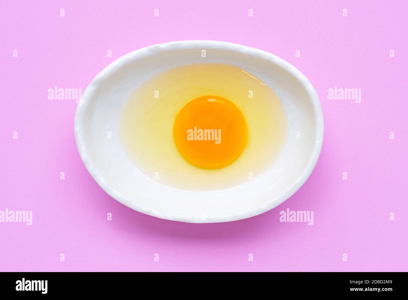 Egg yolk and white in a bowl on pink background. Top view Stock Photo ...