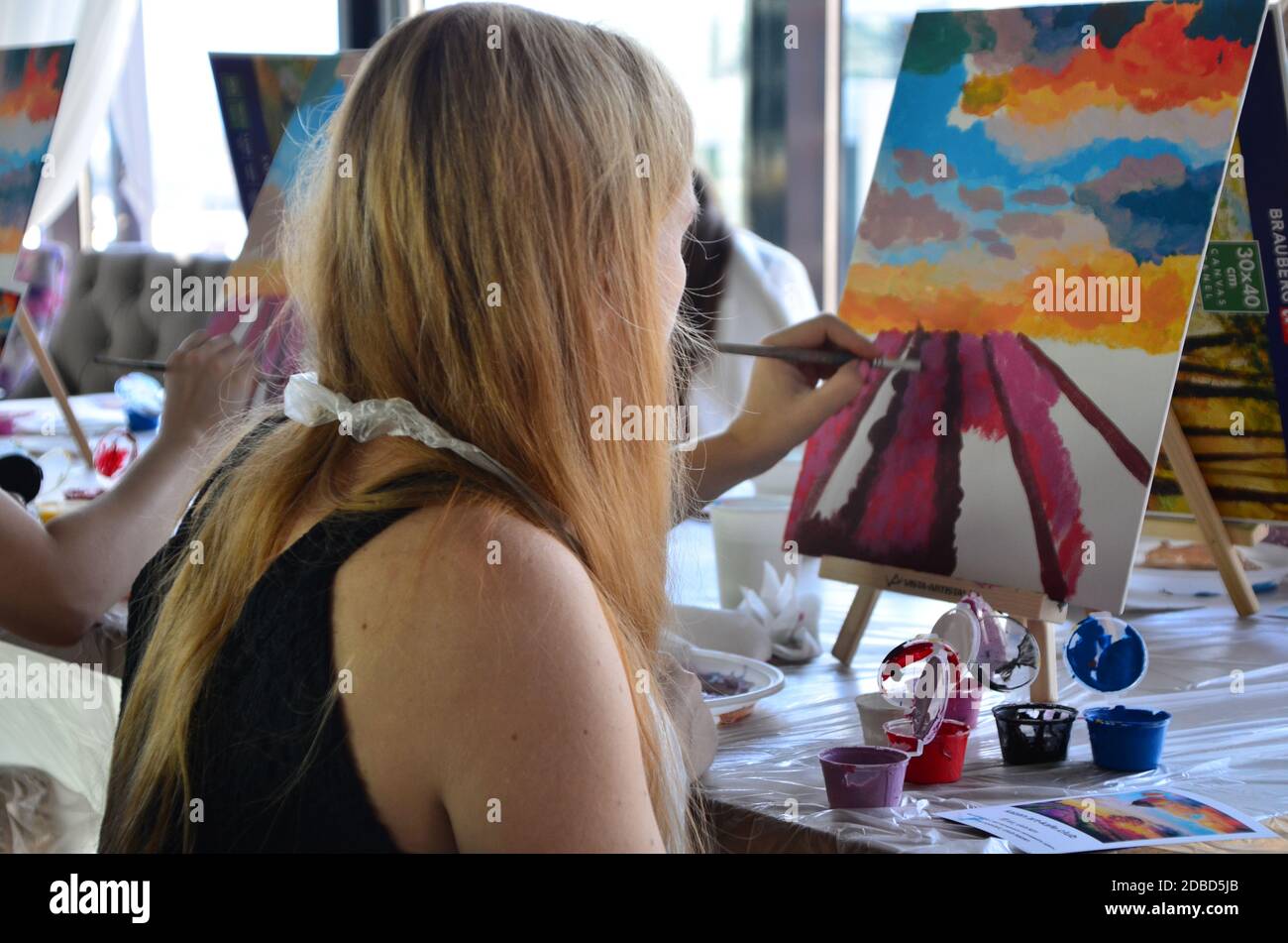 Pretty smiling young woman drawing a picture with paint. Front view on ...