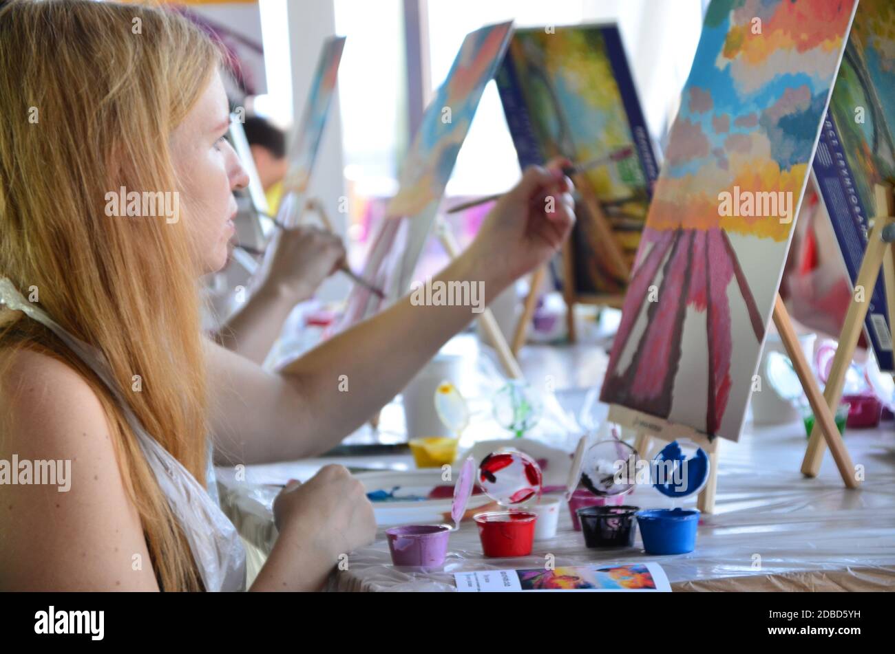 Pretty smiling young woman drawing a picture with paint. Front view on ...