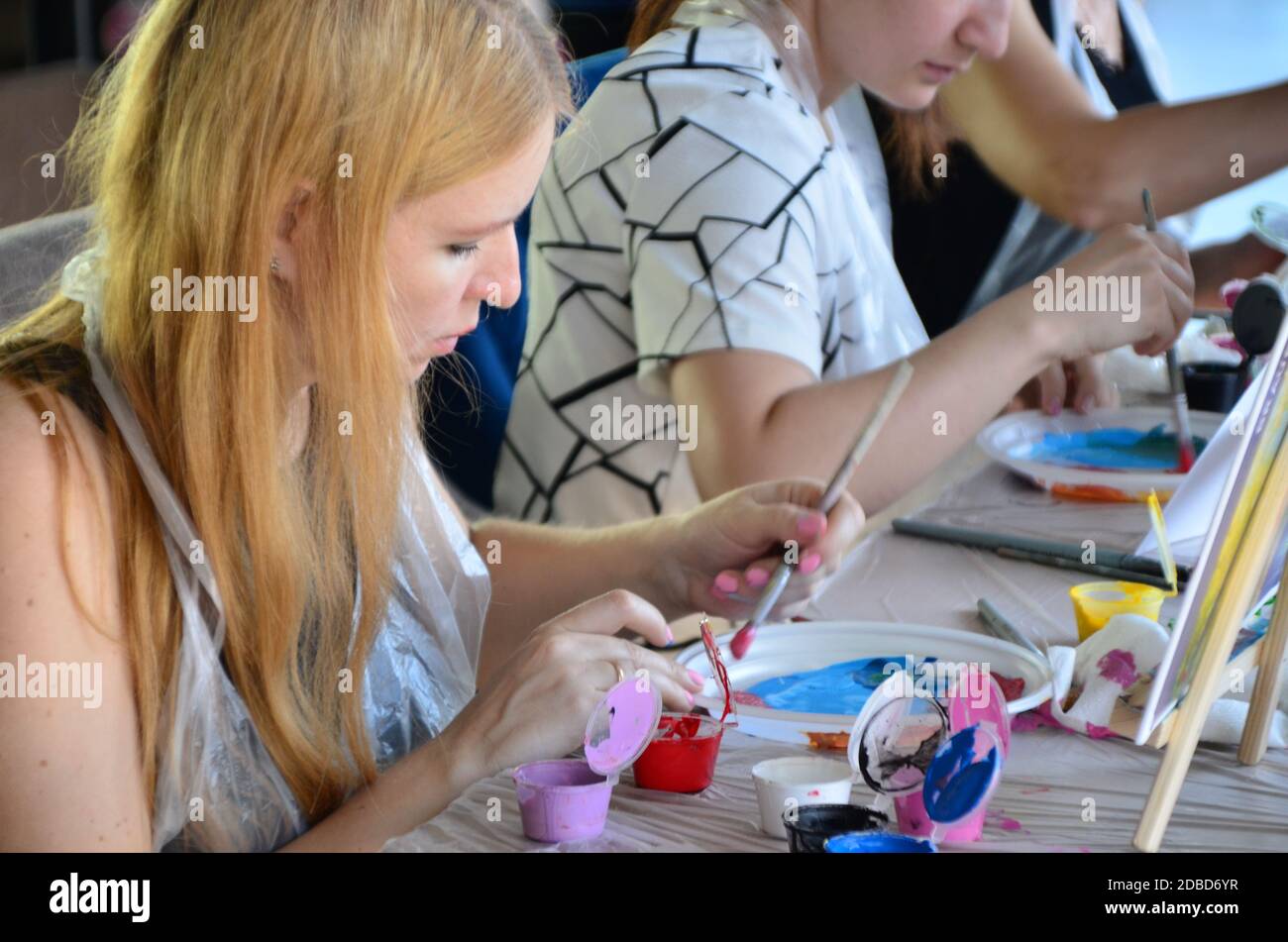Pretty smiling young woman drawing a picture with paint. Front view on ...