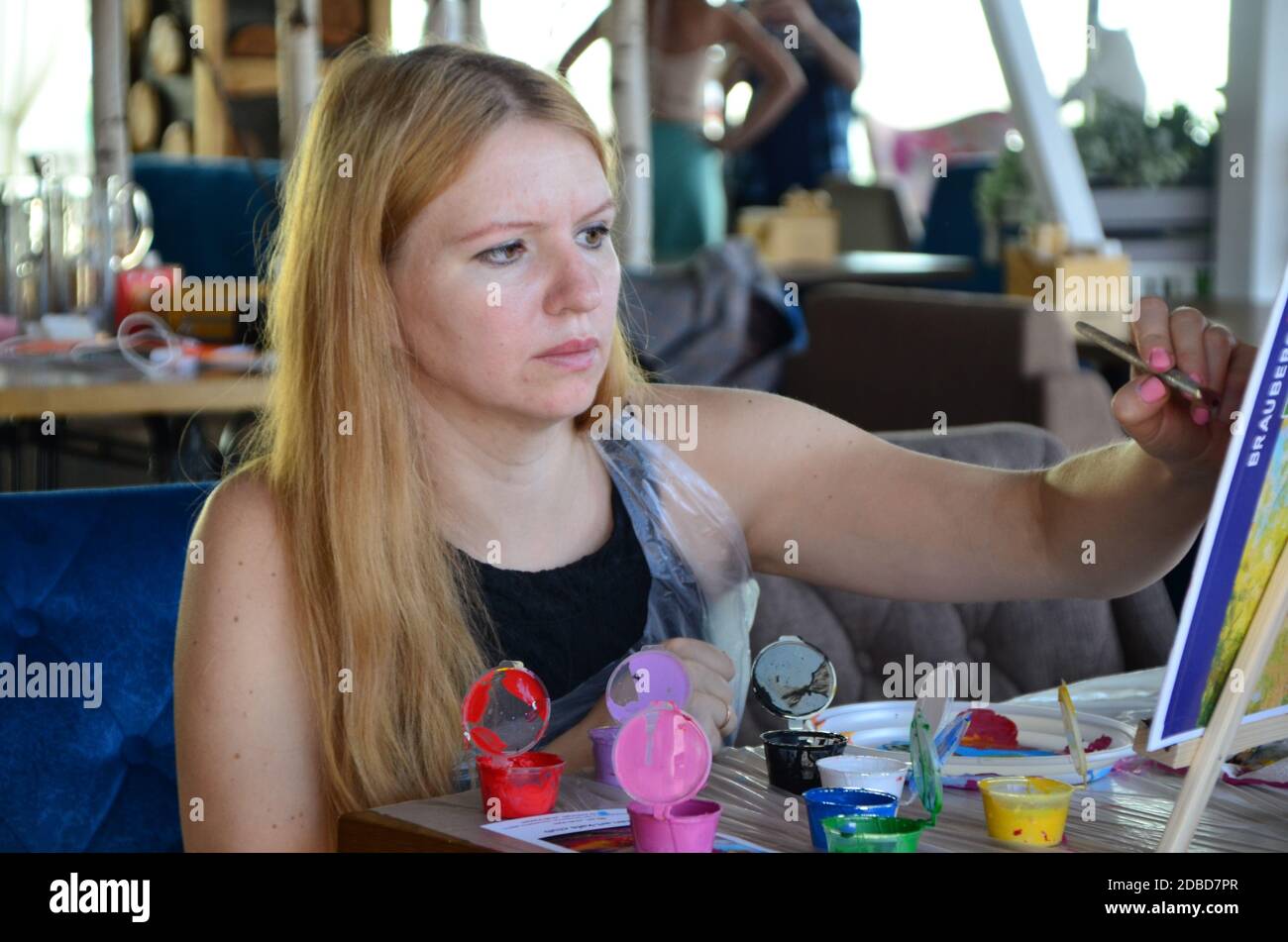 Pretty smiling young woman drawing a picture with paint. Front view on ...