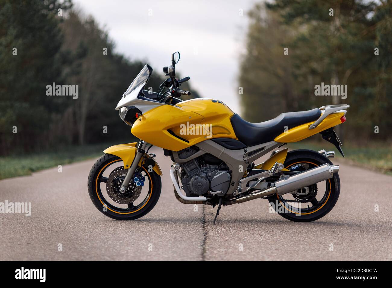 Side view of a yellow motorcycle on a road in a forest area Stock Photo ...