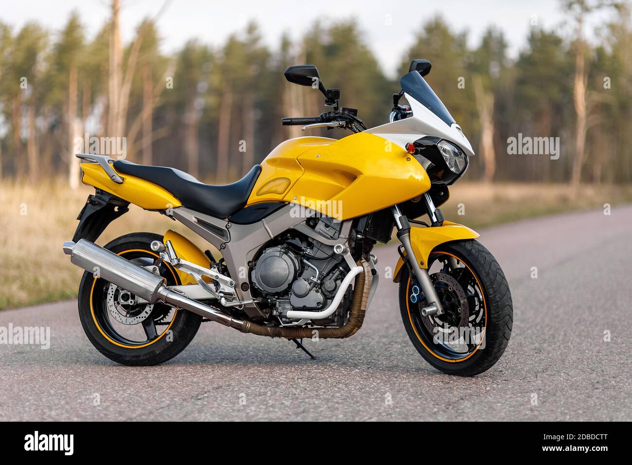 Side view of a yellow motorcycle on a road in a forest area Stock Photo ...