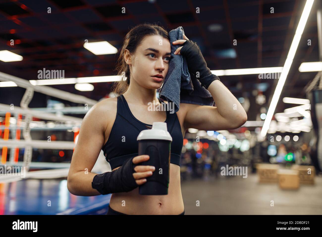 Tired woman wipes her sweat after boxing training, ring on background ...