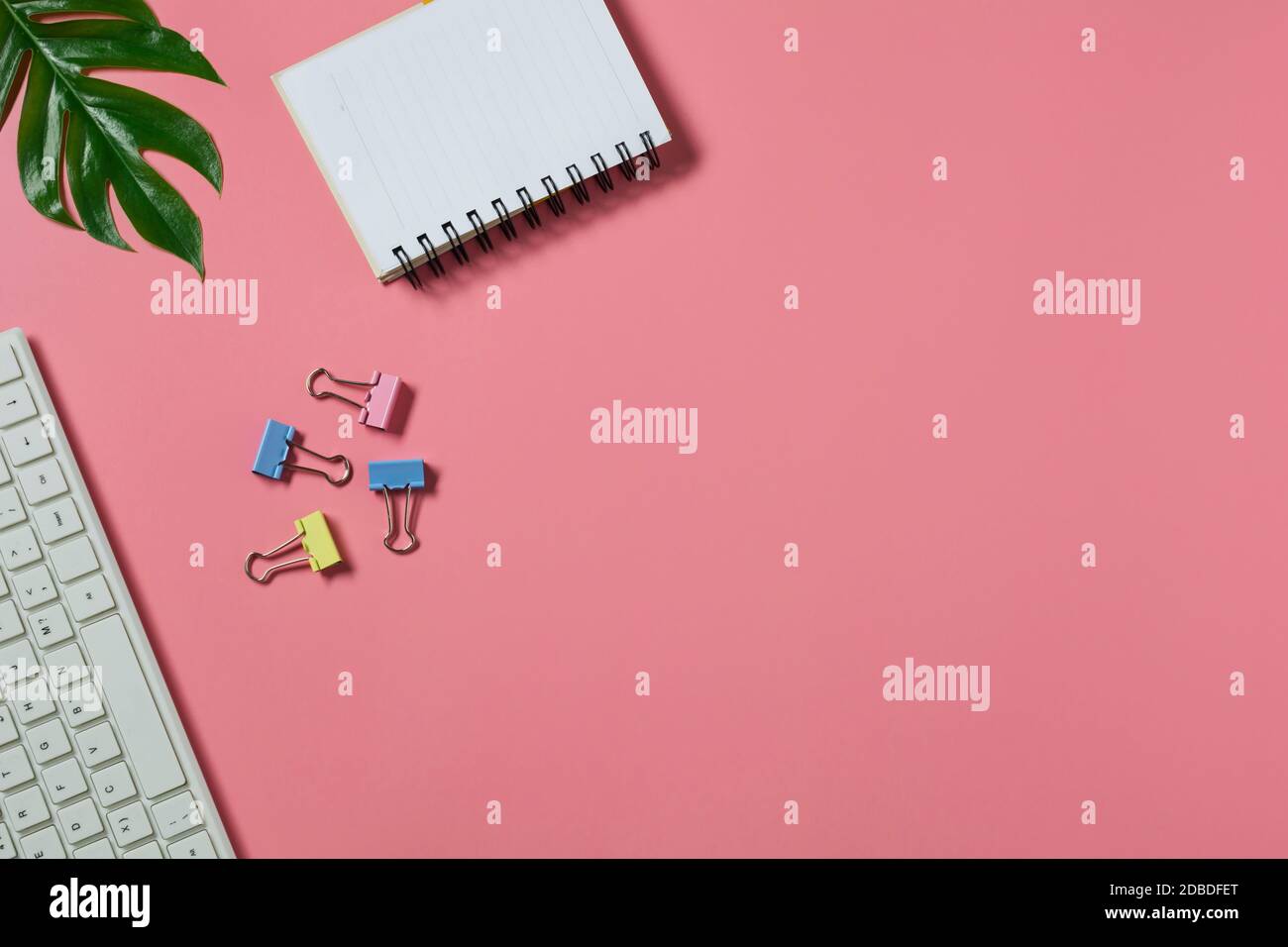 Top view with the keyboard and notebook on pink backgroup. Cluttered ...