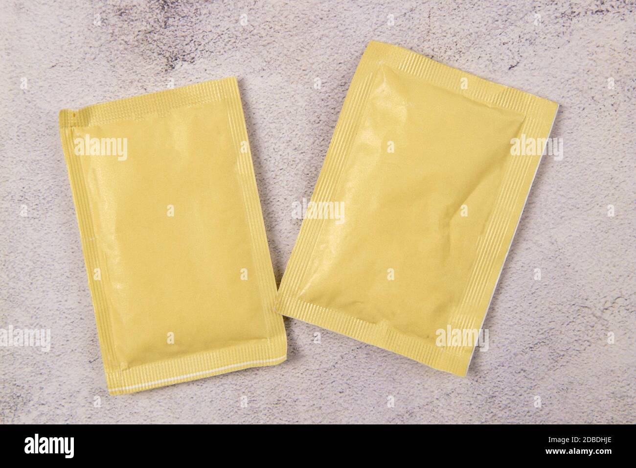 Two white paper sachets isolated on marble background. Top views with ...