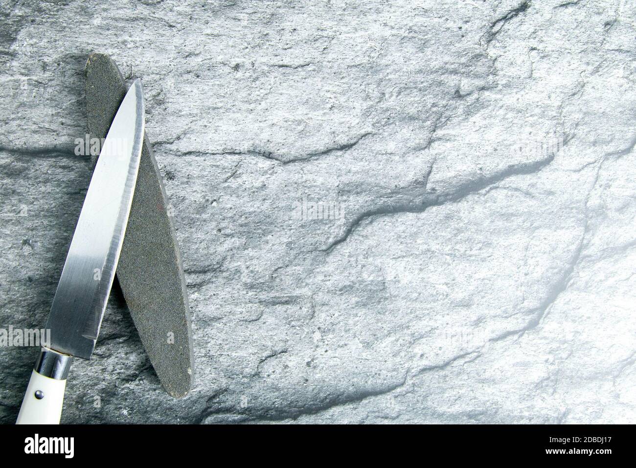 Knife and sharpening stone on grey marble background. Top views with ...