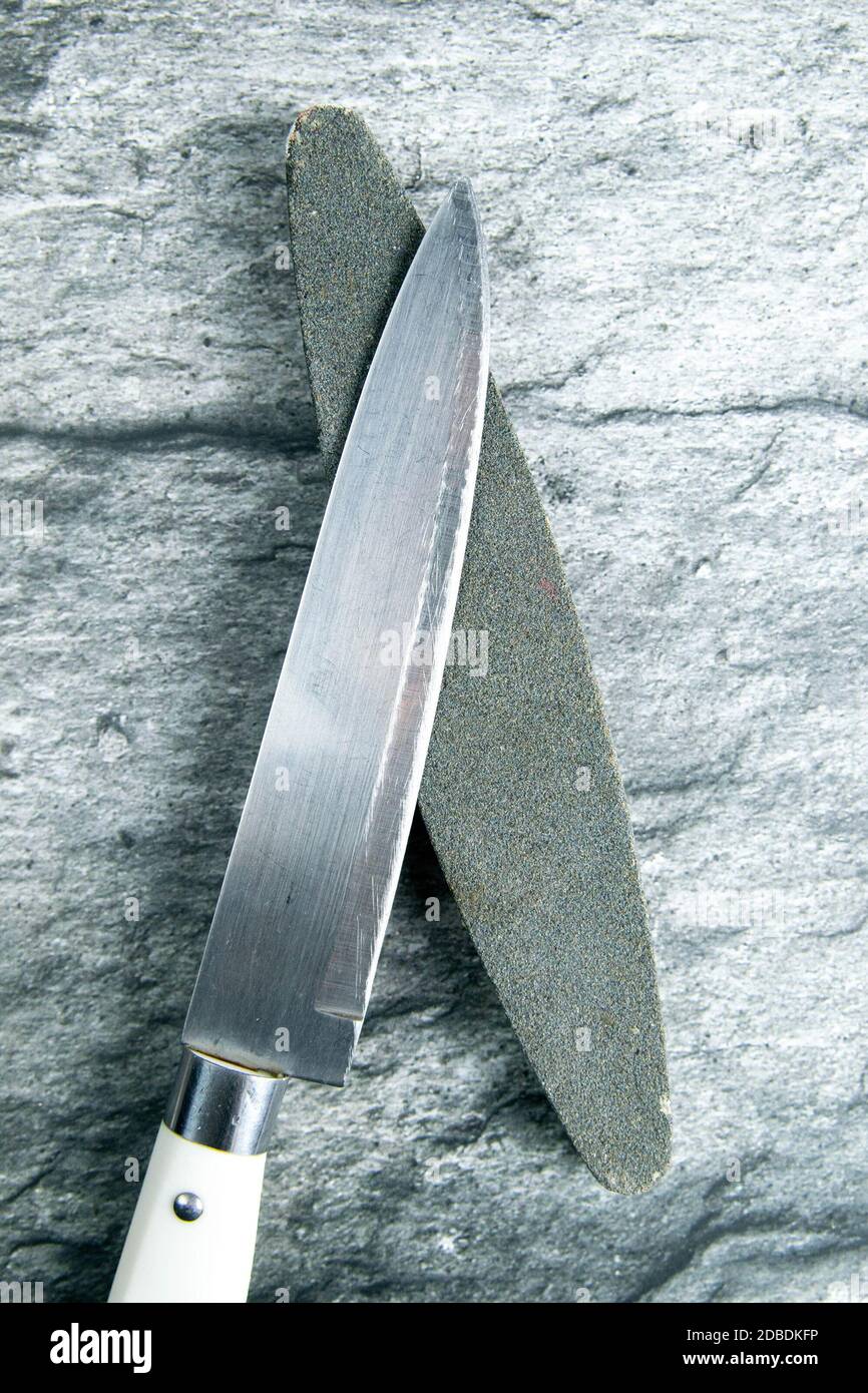 Knife and sharpening stone on grey marble background. Top views, close ...