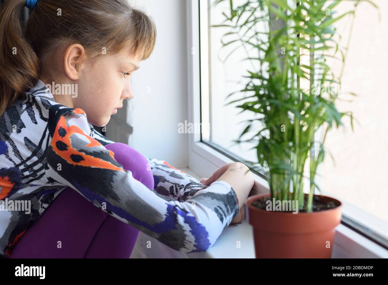 Upset girl sitting by the window and looking very sad out the window ...