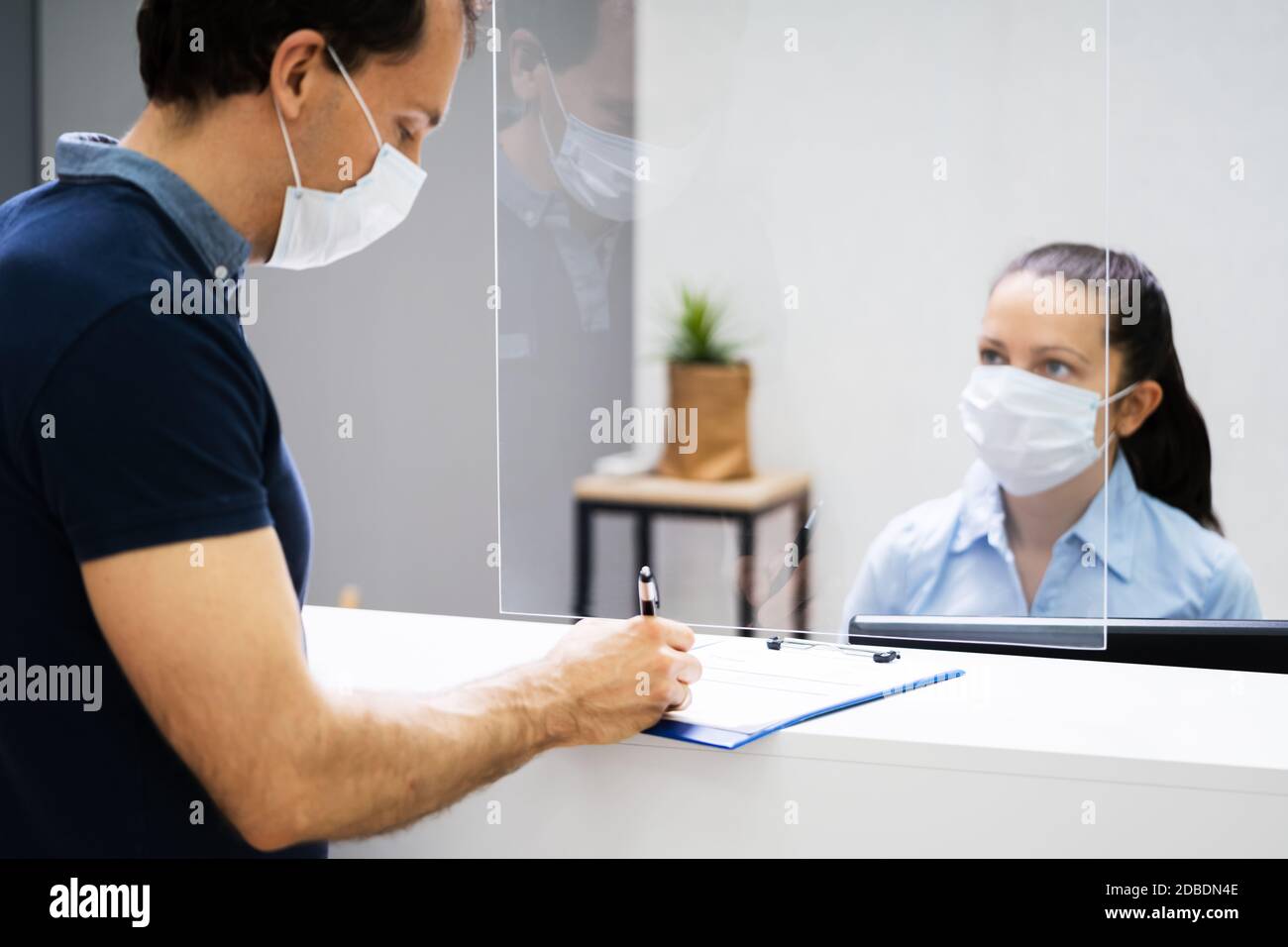 Client Signing Paper At Reception Desk In Face Mask Stock Photo - Alamy