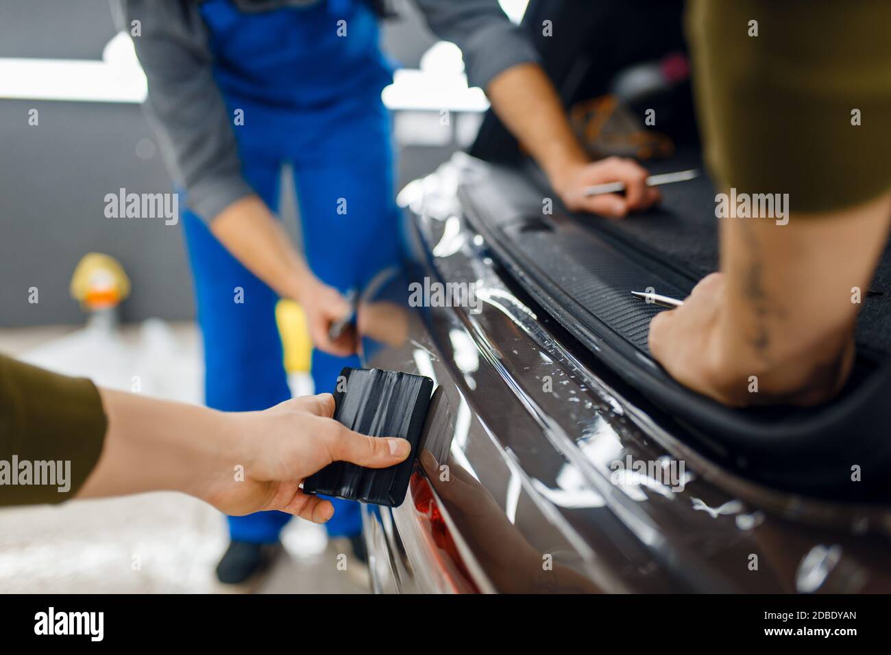 Two workers smoothes car protection film on rear bumper. Installation ...