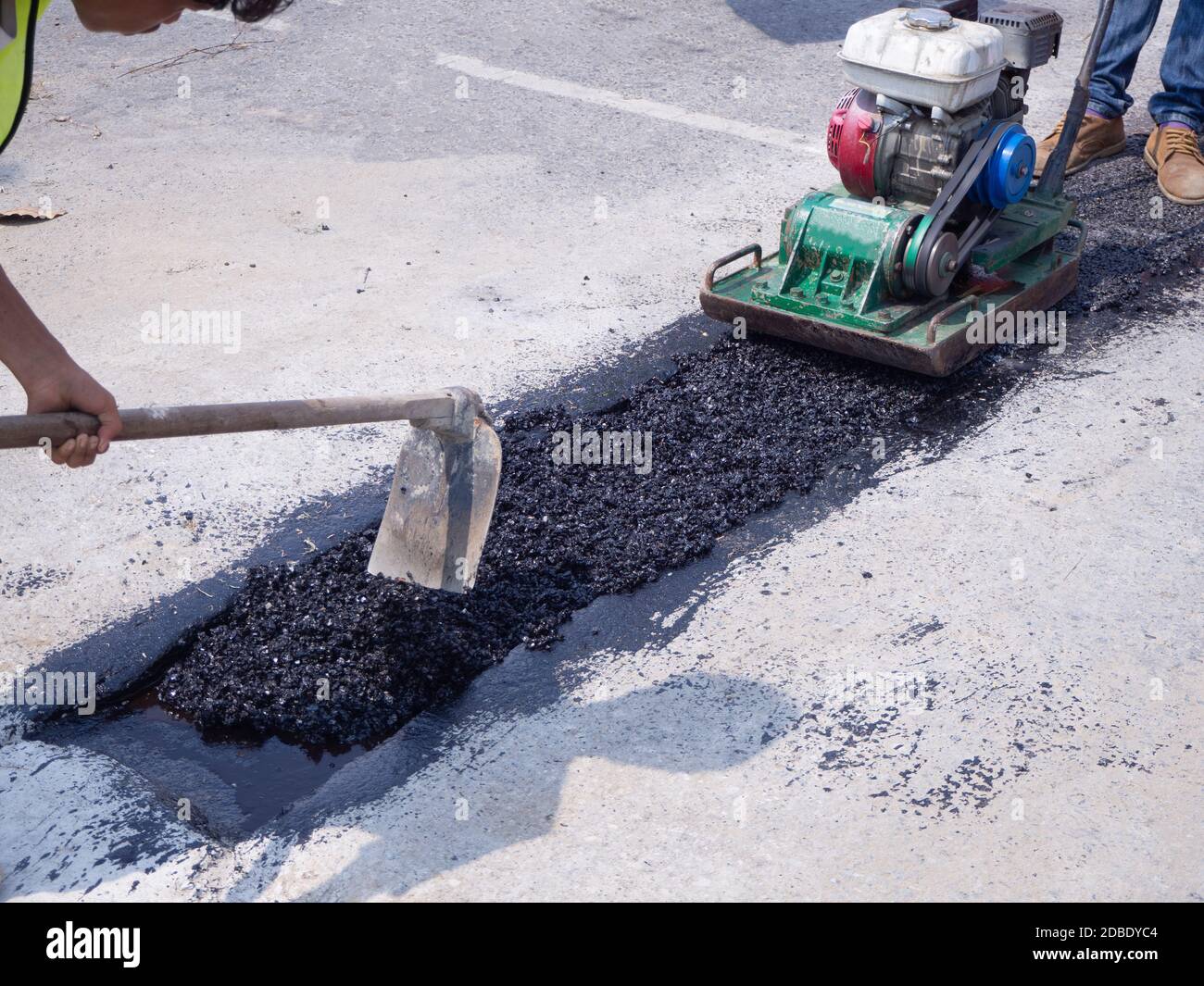 Worker use vibratory plate compactor compacting asphalt at road repair ...