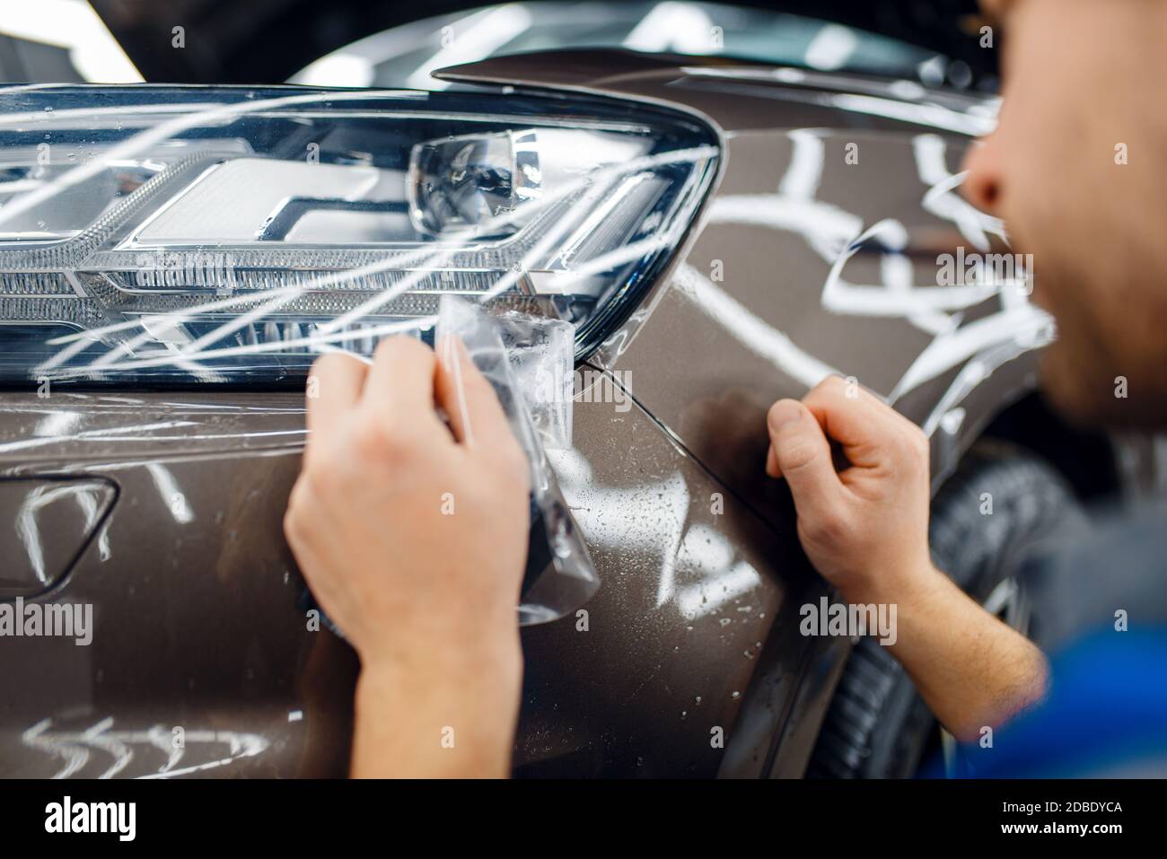 Male worker installs transparent protection film on car headlight ...