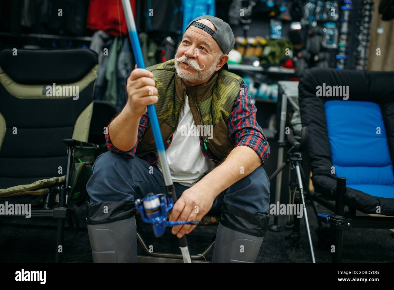Male angler in rubber boots holds rod in fishing shop, first-person ...