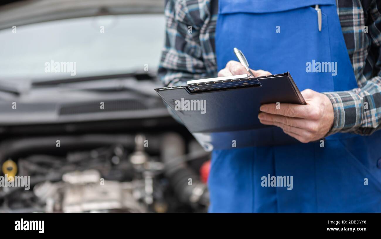 Car mechanic checking a car engine and writing on clipboard Stock Photo ...