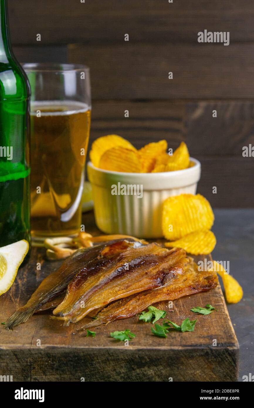 Dried blue whiting fish with beer, lemon and potato chips on dark ...