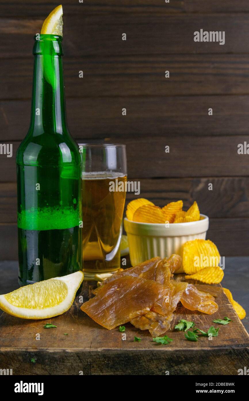 Dried catfish fillet with beer, lemon and potato chips on dark wooden ...