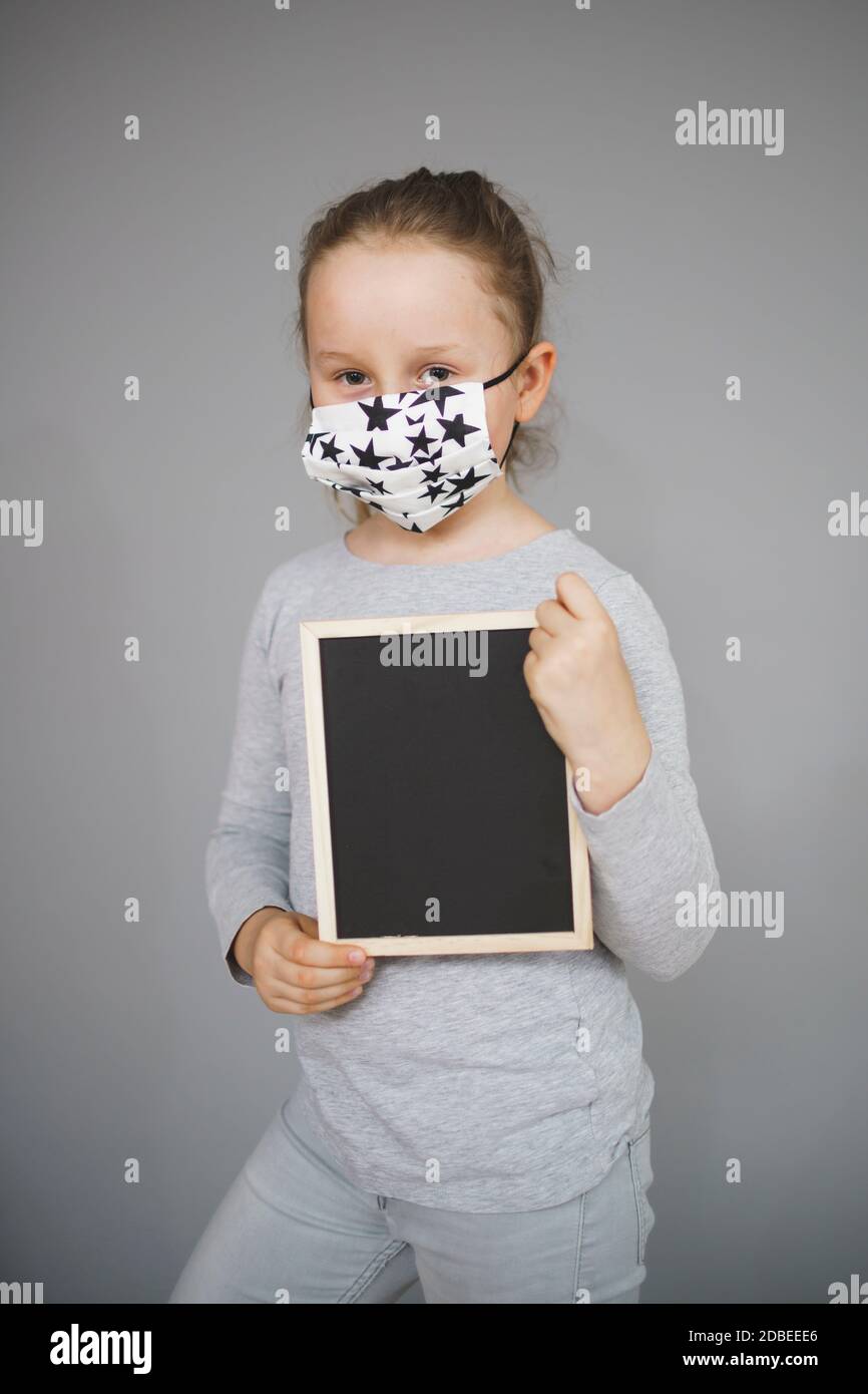 girl with message board and nose mouth mask is posing in front of grey ...