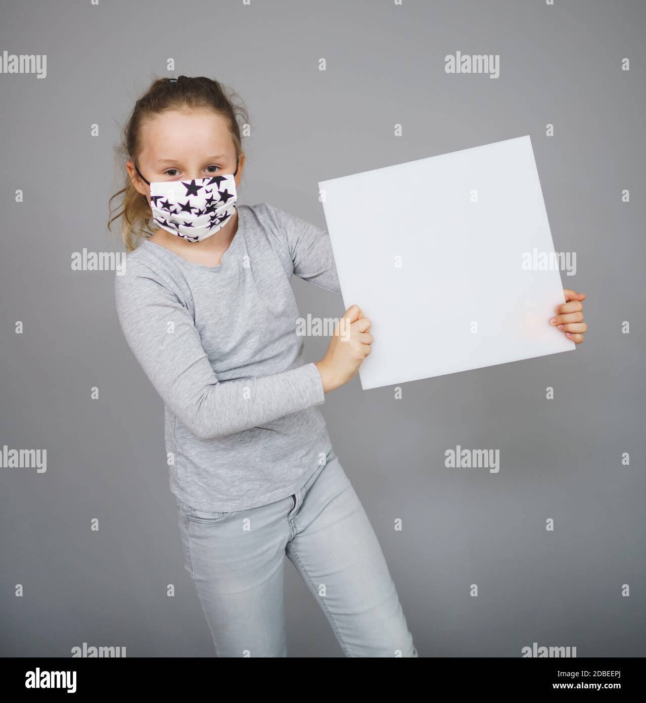 girl with message board and nose mouth mask is posing in front of grey ...