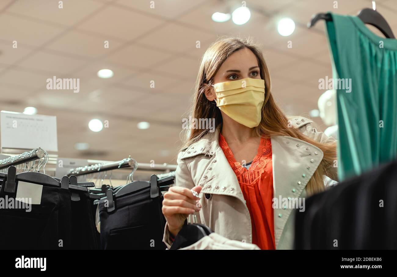 Woman shopping in fashion store wearing face mask looking at some ...