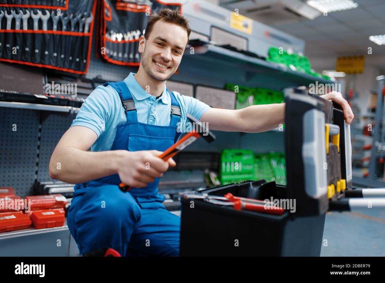 Happy male worker in uniform choosing toolbox in tool store. Choice of ...