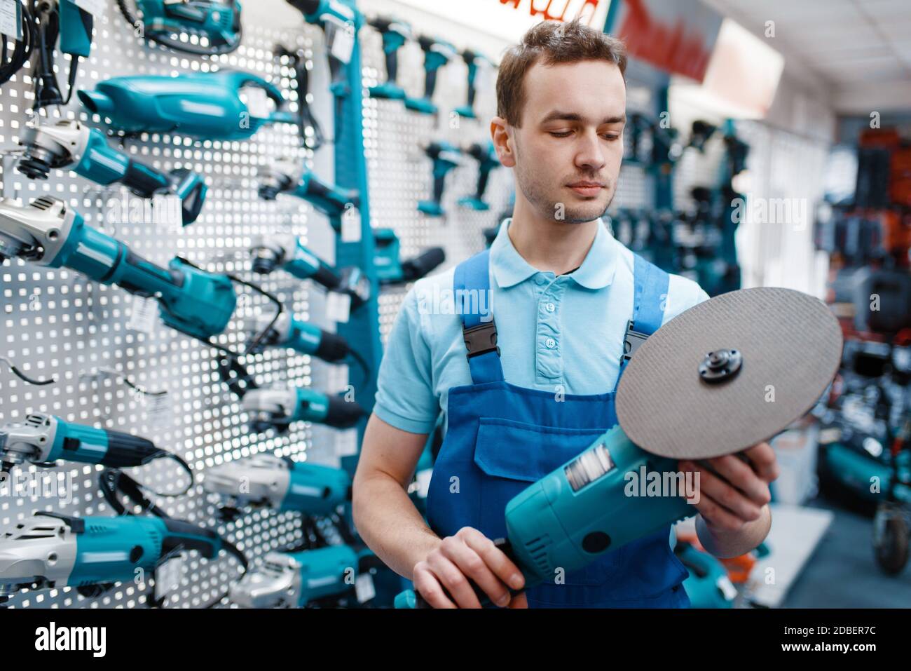 Male worker in uniform holds angle grinder in tool store. Choice of ...